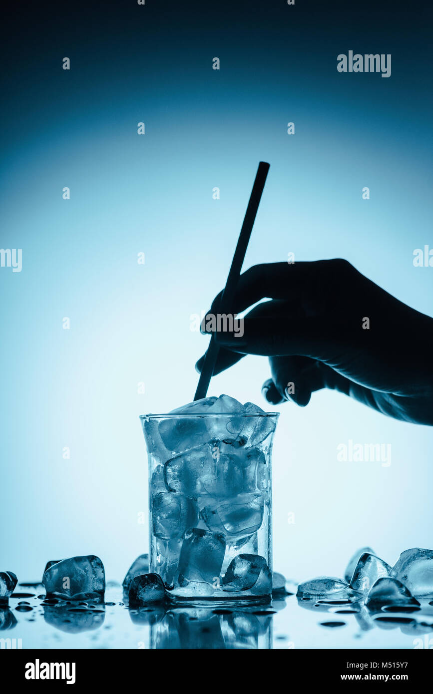 cropped view of person with straw and full glass on melting ice cubes ...