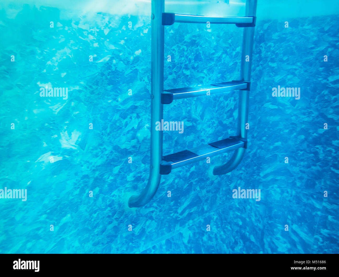 Three steps of metal swimming pool steps seen from under the water in a ...