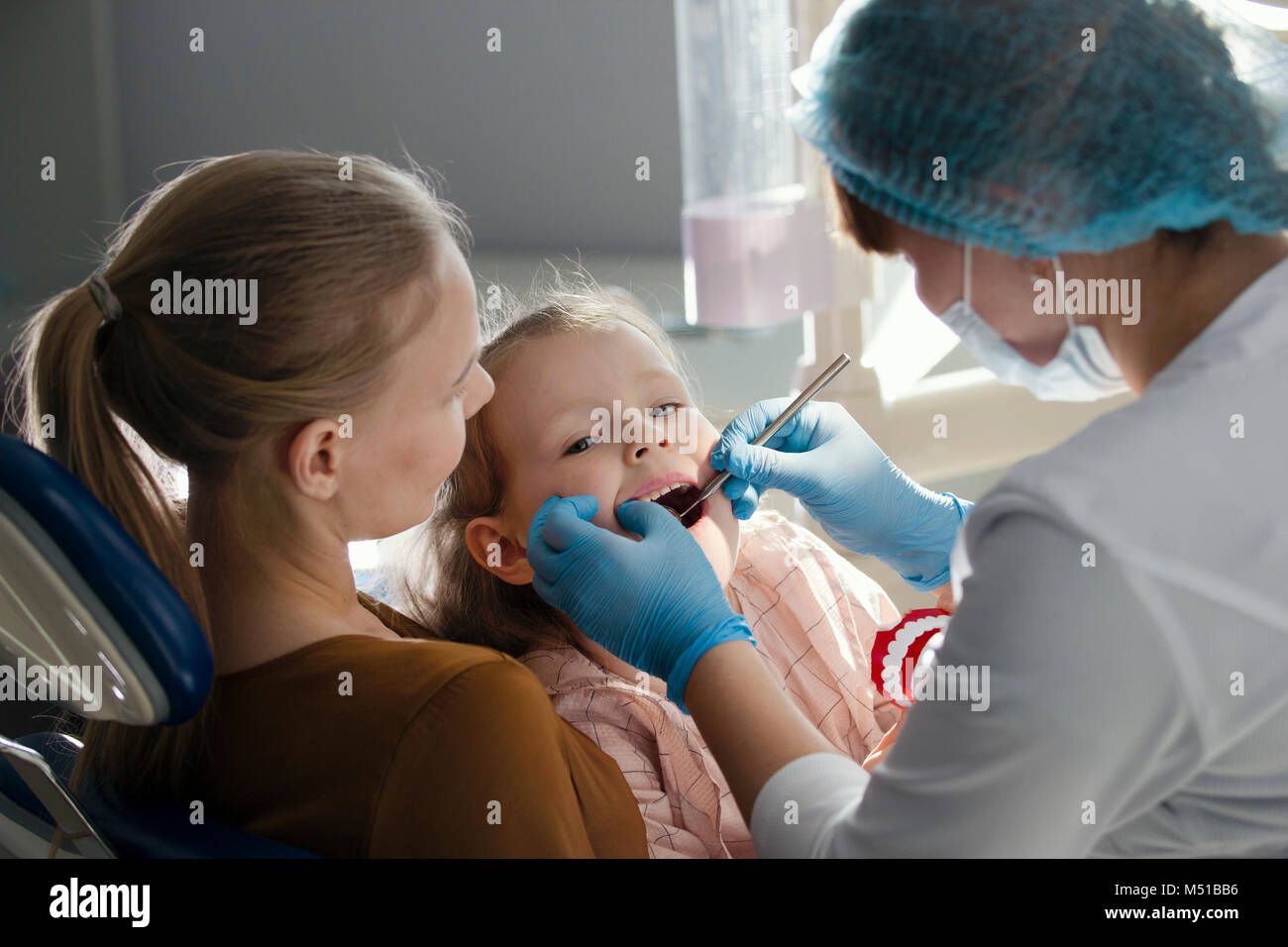 Little girl with mommy in dentist room - doctor examines the girl's ...