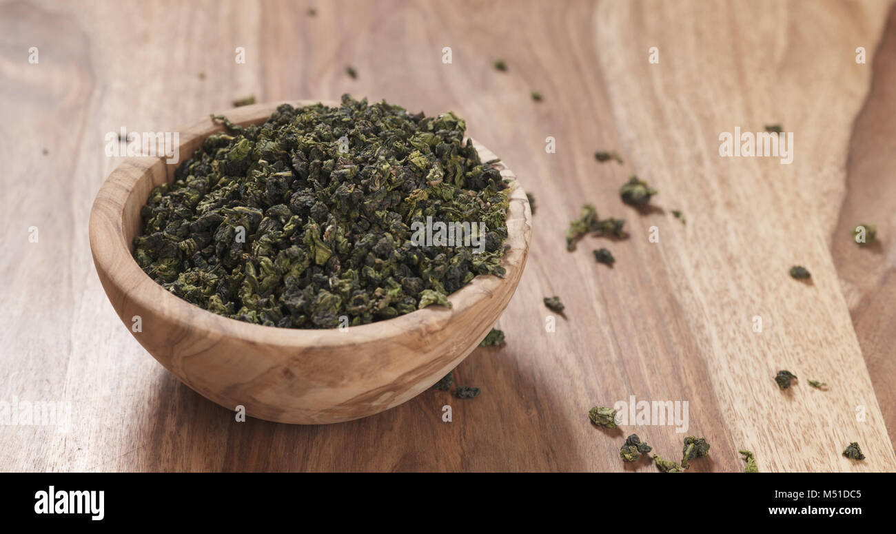 dried green tea leaves falling into wood bowl on table, wide photo ...