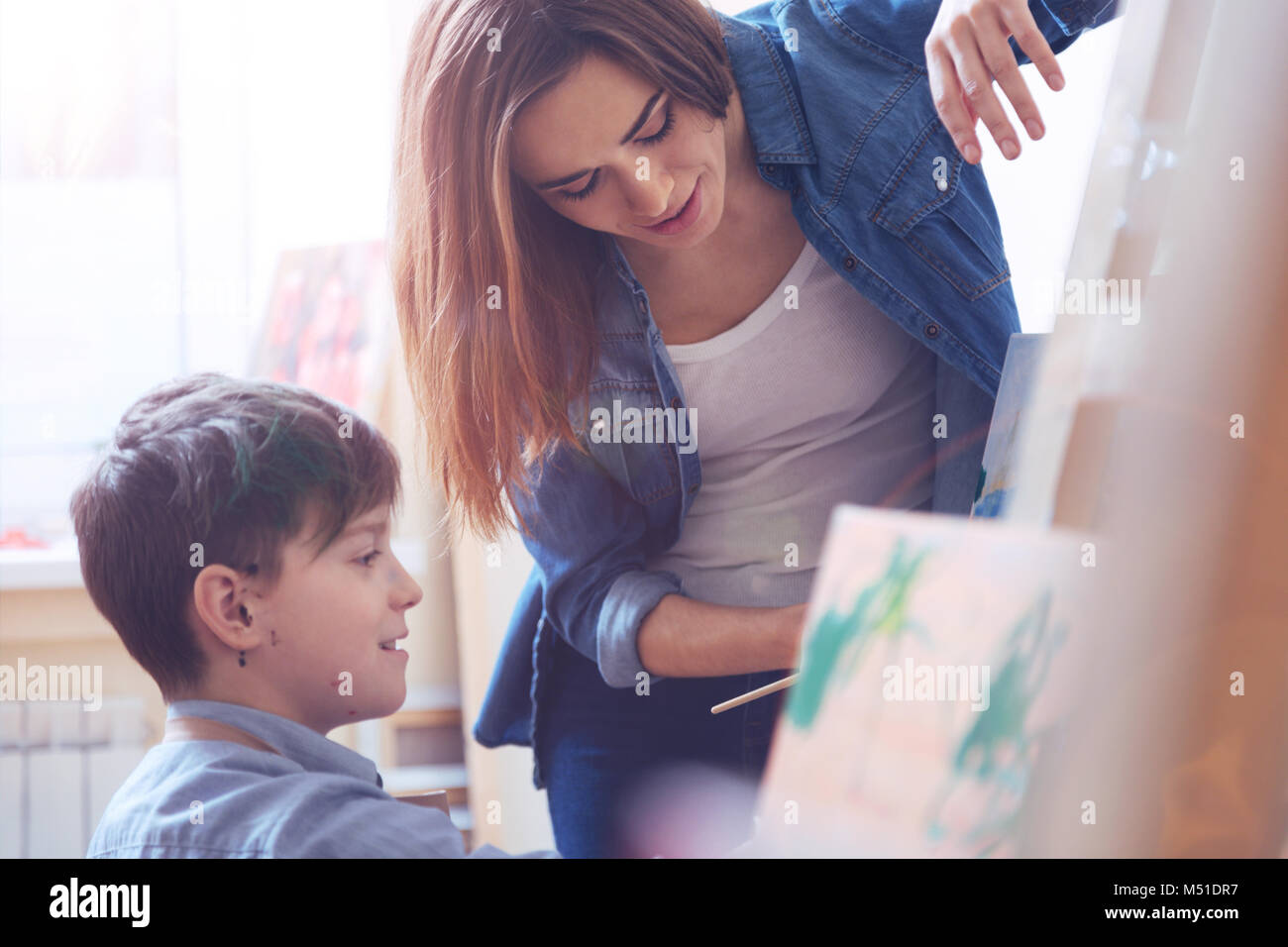 Pensive female artist helping kid at painting class Stock Photo - Alamy