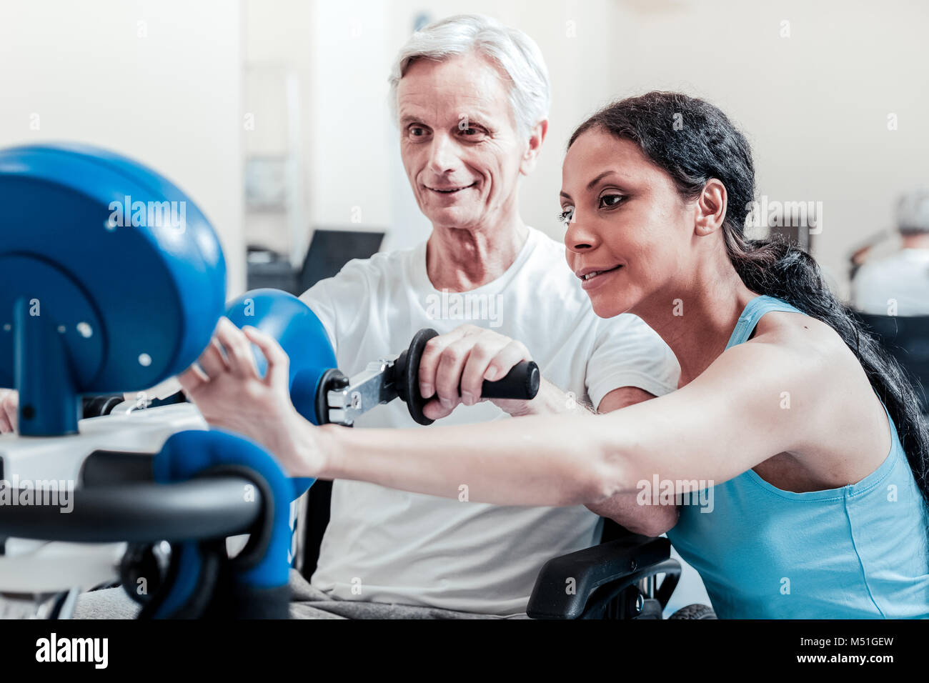Smiling trainer setting a training device for an old man Stock Photo ...