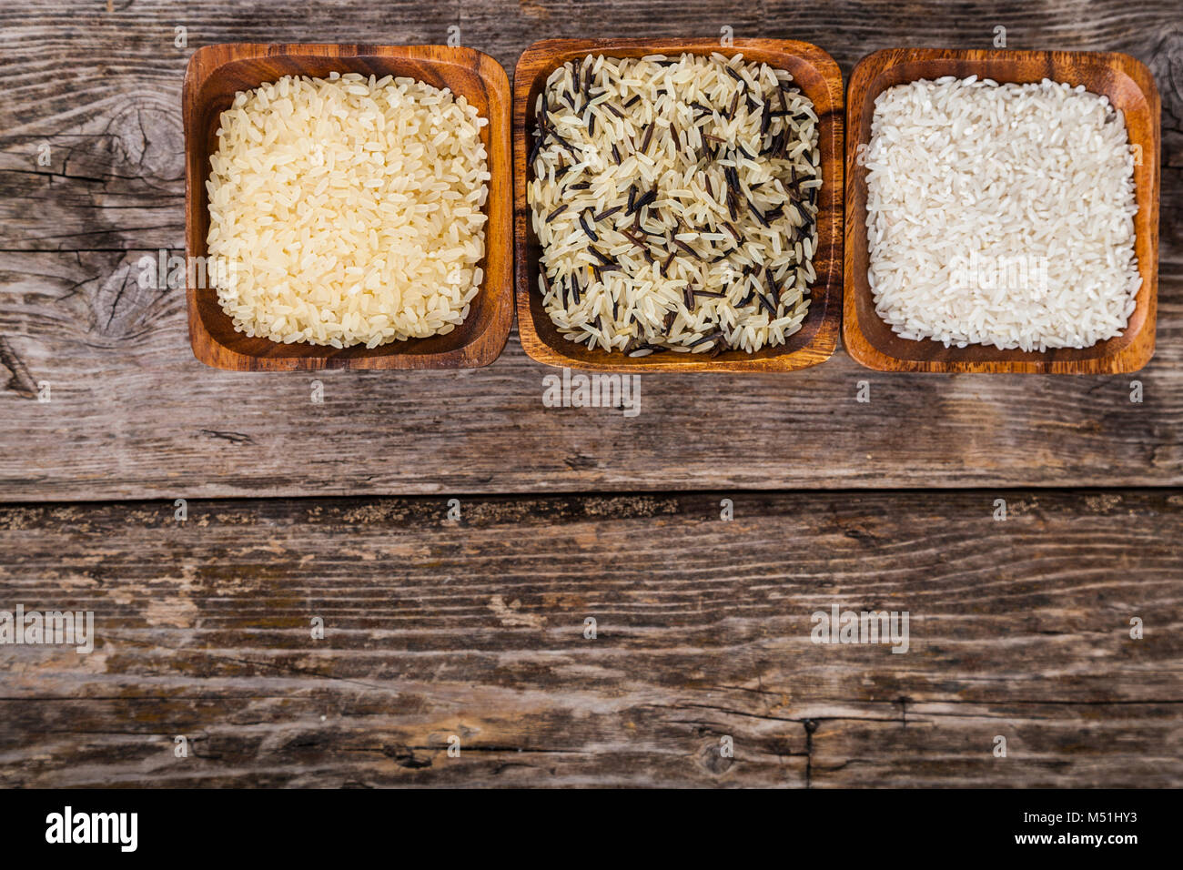Three bowls with different varieties of rice on a wooden background ...