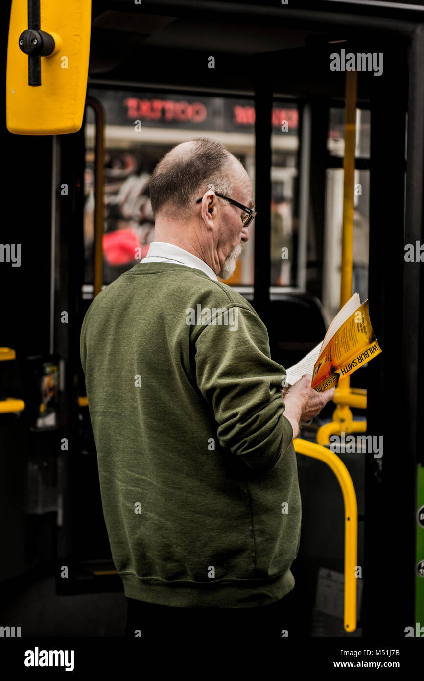 A bored bus driver waiting for passengers to arrive while reading his ...