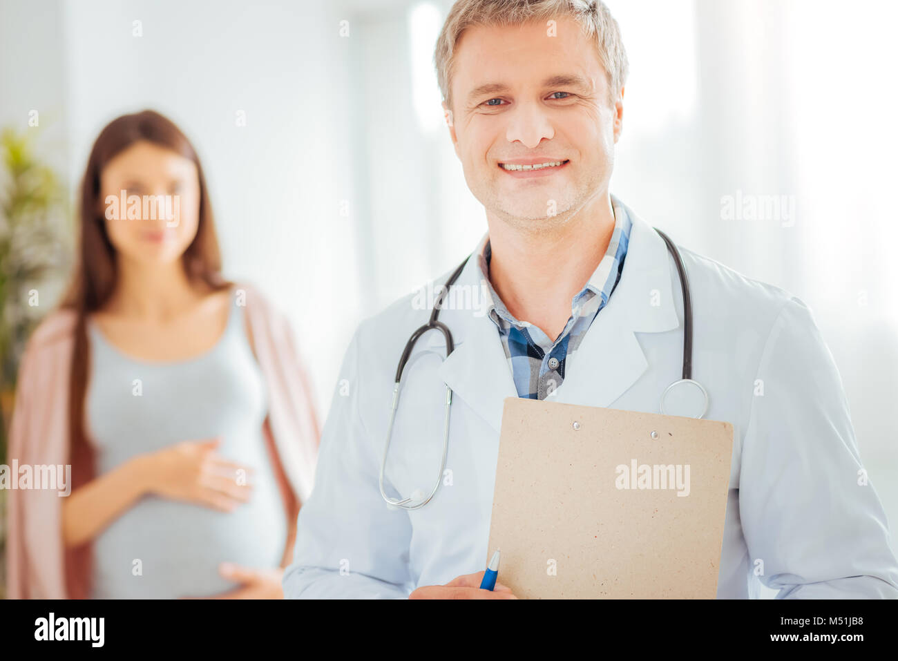 Cheerful doctor smiling while holding clipboard Stock Photo - Alamy