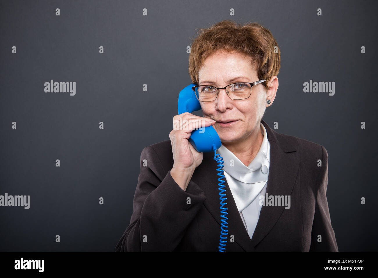 Business senior lady speaking at big blue telephone receiver on black ...