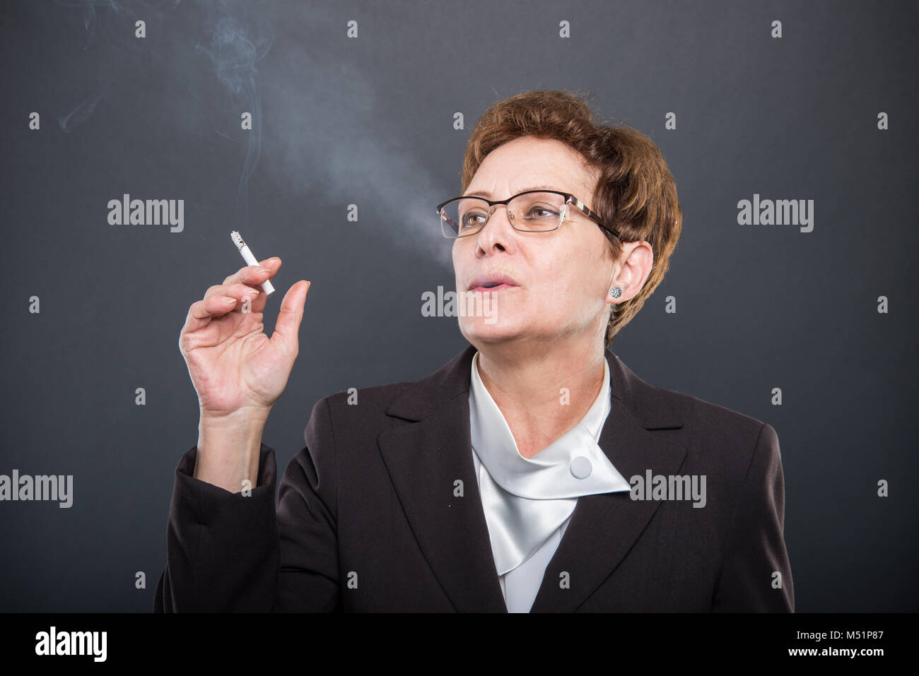 Business senior lady enjoying smoking cigarrete on black background ...