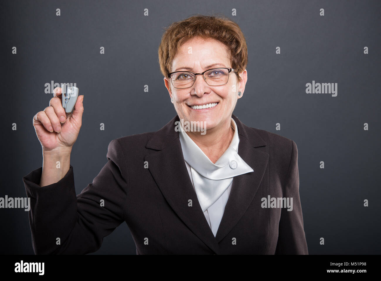 Business senior lady holding stapler and smiling on black background ...