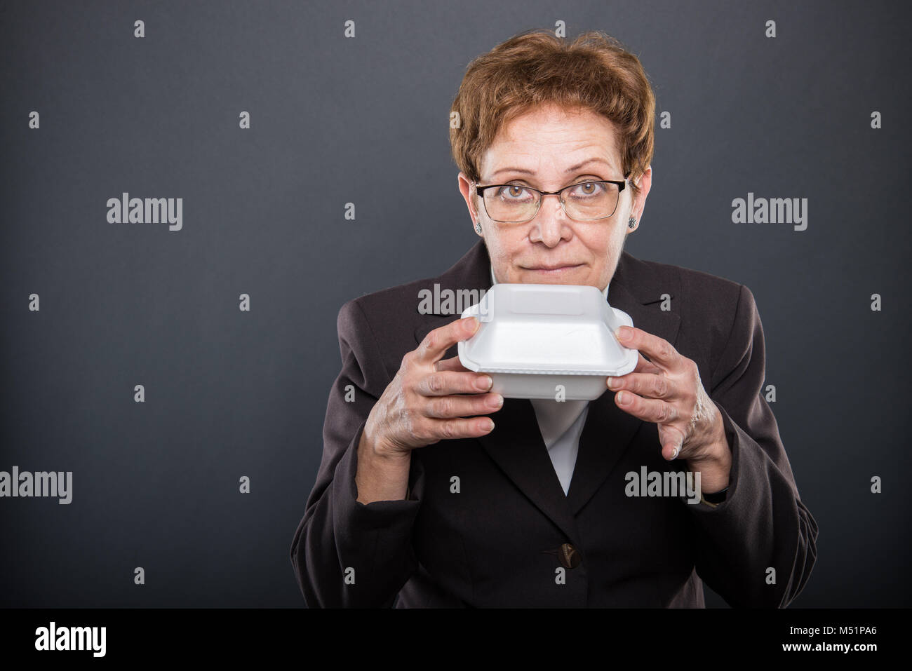 Portrait of business senior lady smelling lunch box on black background ...