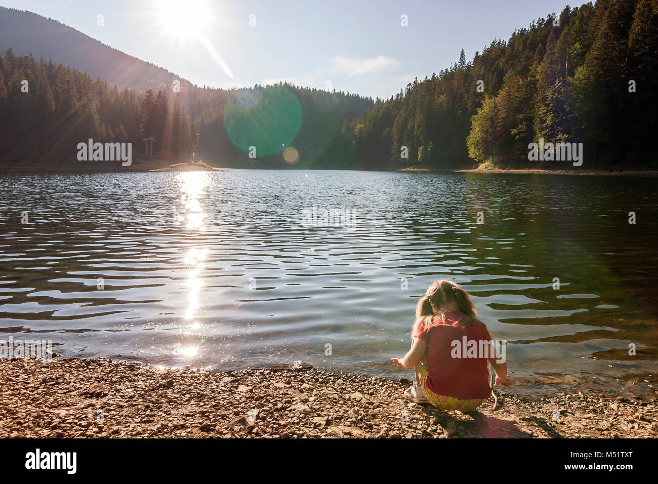 A cute little girl plaing on the bank of a mountain lake on a warm ...
