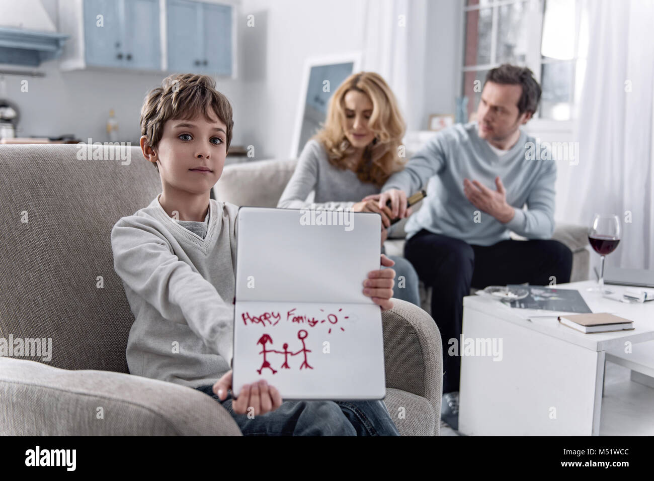 Optimistic boy drawing a happy family while his parents quarreling ...
