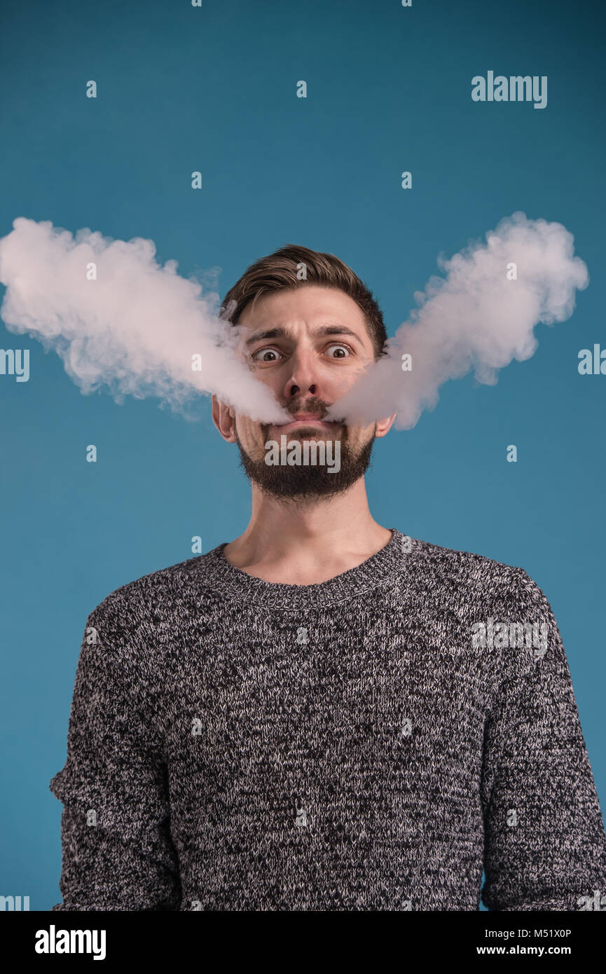 Handsome expressive man vaping against blue background Stock Photo - Alamy