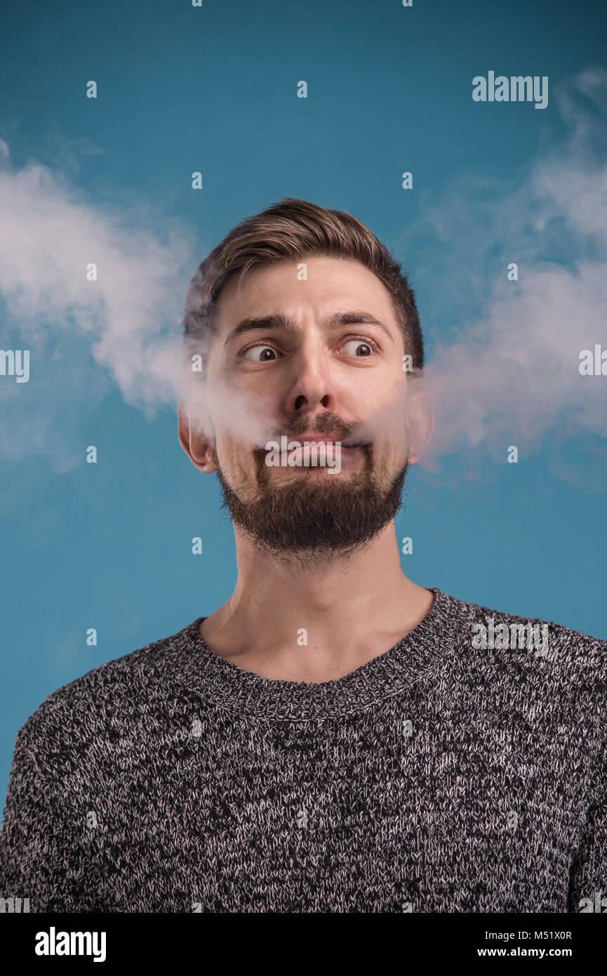 Handsome expressive man vaping against blue background Stock Photo - Alamy