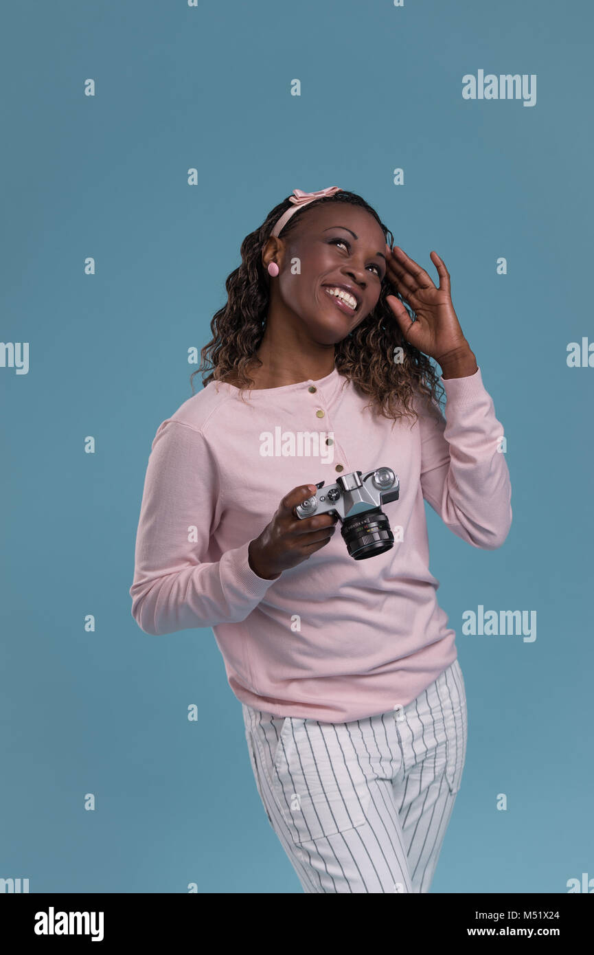 Beautiful young african woman using camera and photographing on blue ...