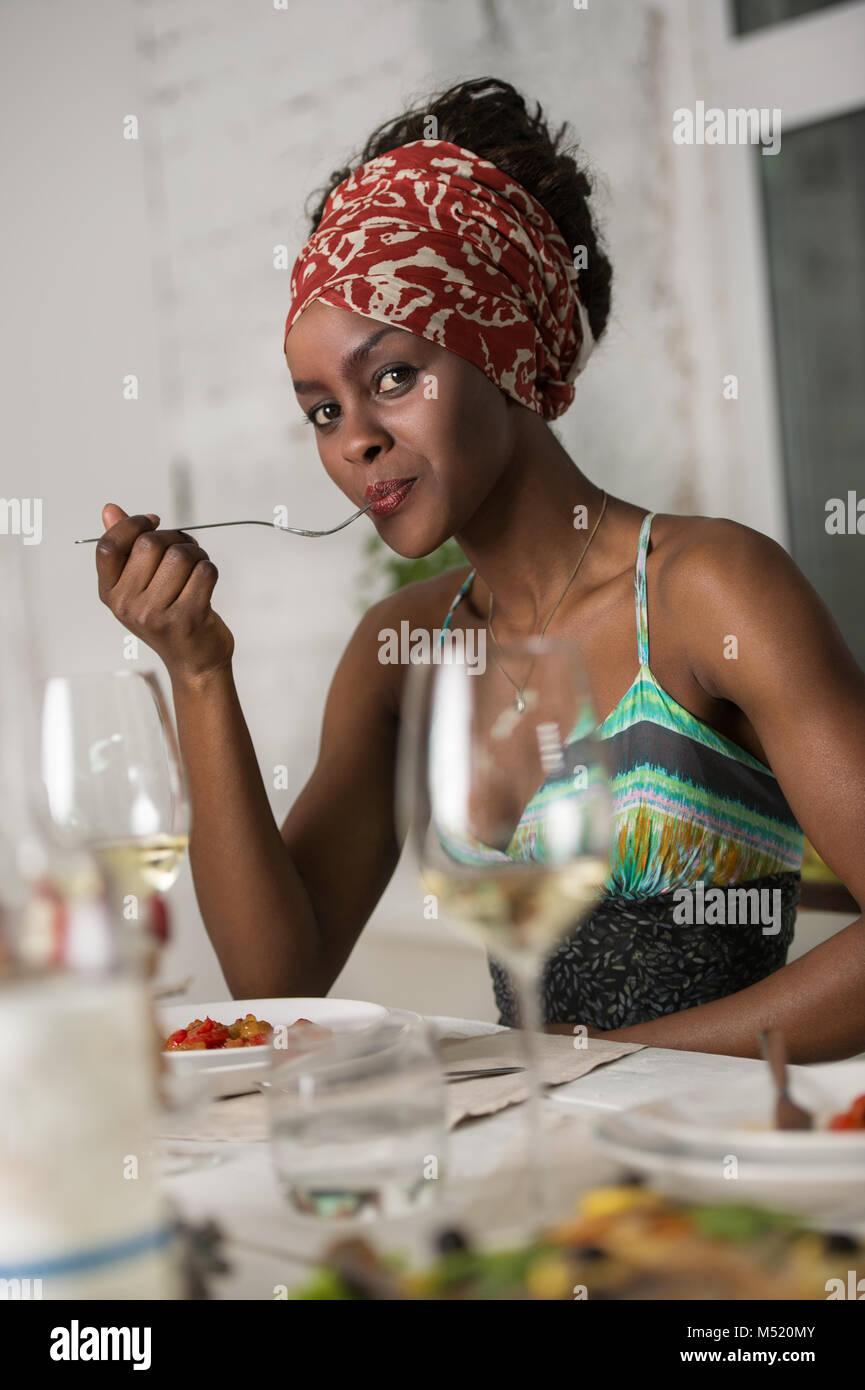 African woman eating at home and drinking wine and looking very happy ...