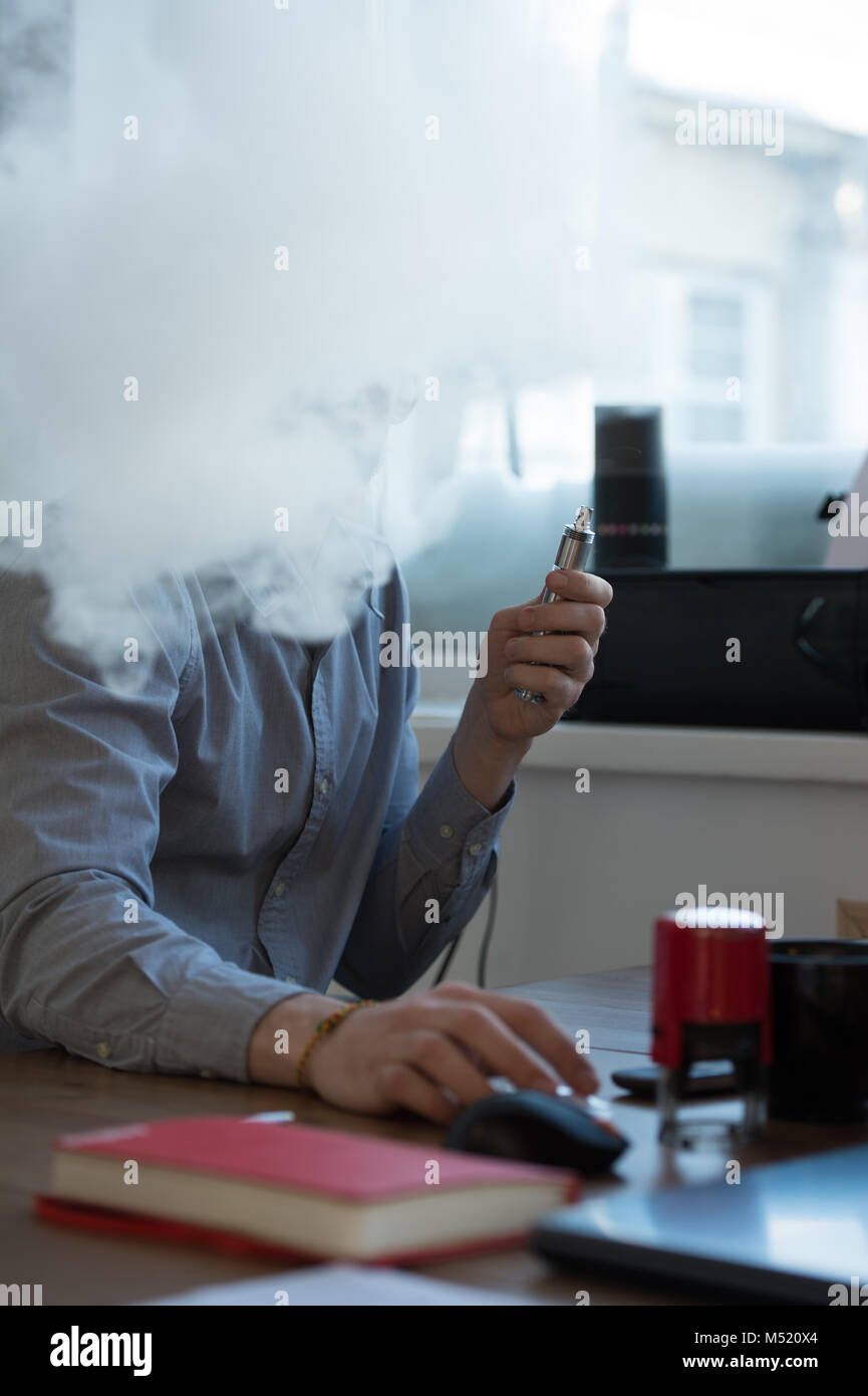 Handsome businessman working with computer in office and vaping ...