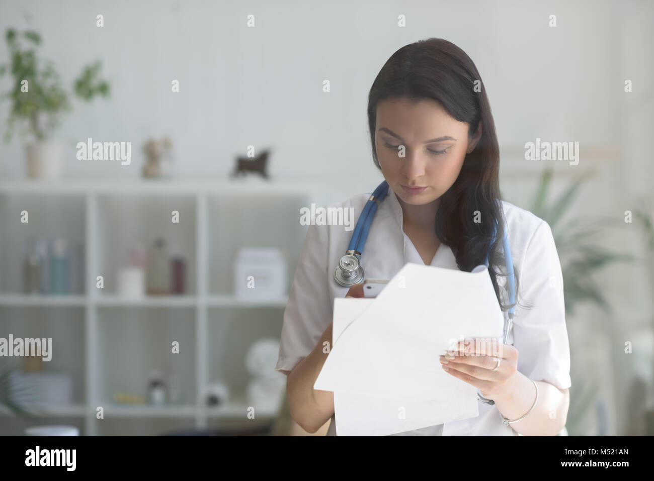 Doctor at her medical office using mobile phone and holding papers ...