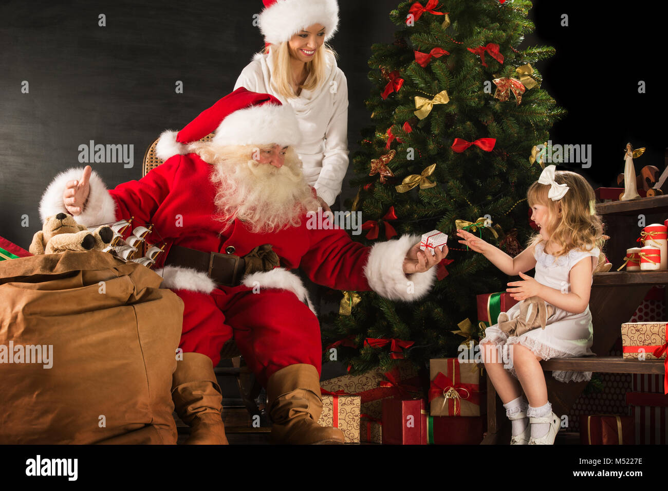 Photo of cute girl and her mother and Santa Claus at home near ...
