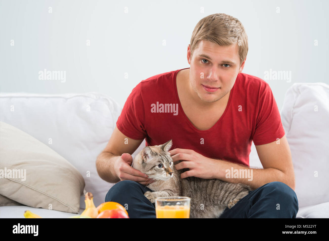 Man and a cat at home. Handsome man cuddling his tabby cat on sofa ...