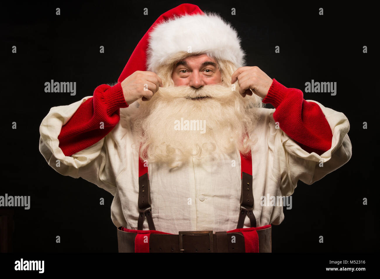 Photo of happy Santa Claus touching mustache and looking at camera on ...