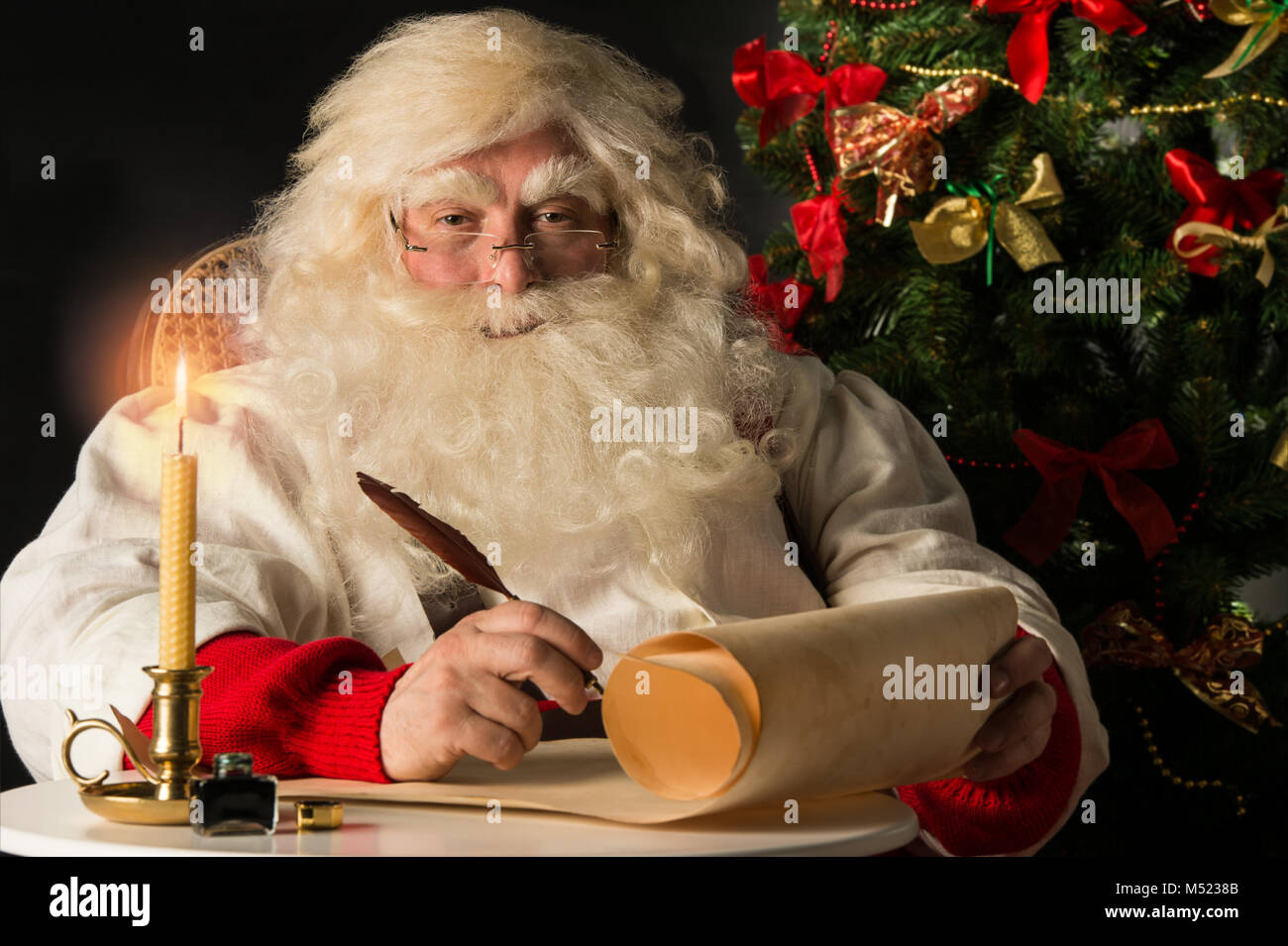 Santa Claus sitting at home and writing on old paper roll to do list ...