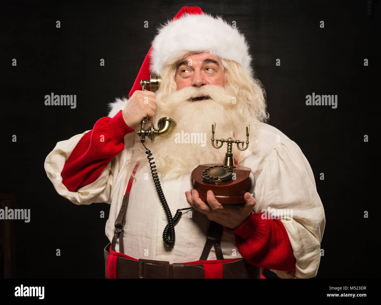 Portrait of happy Santa Claus calling phone against dark background ...