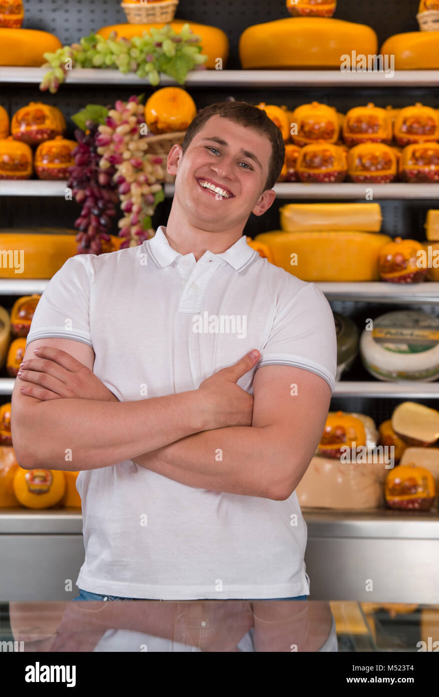 Handsome male owner of a cheese store standing with folded arms looking ...
