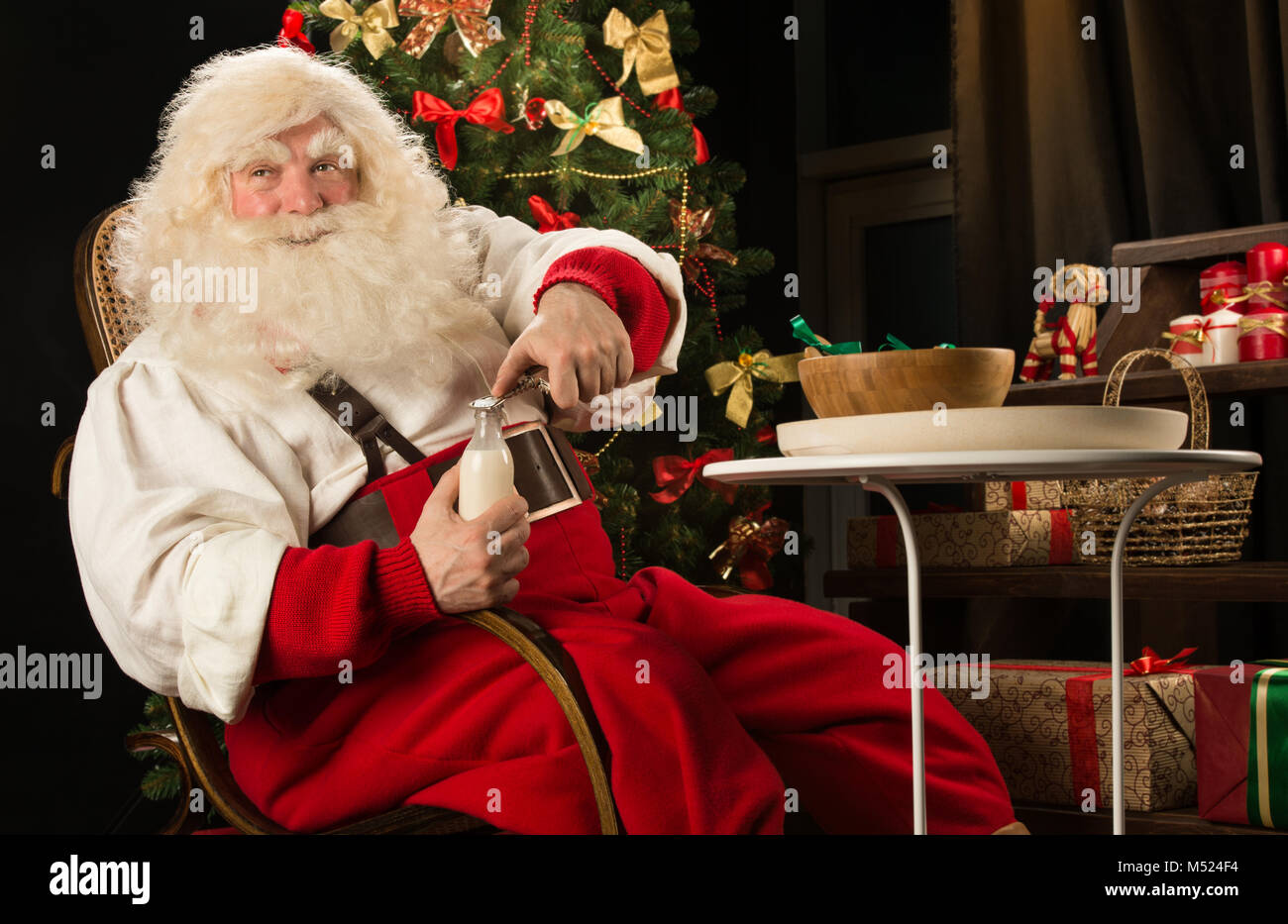 Santa Claus eating cookies with milk sitting near Christmas tree ...