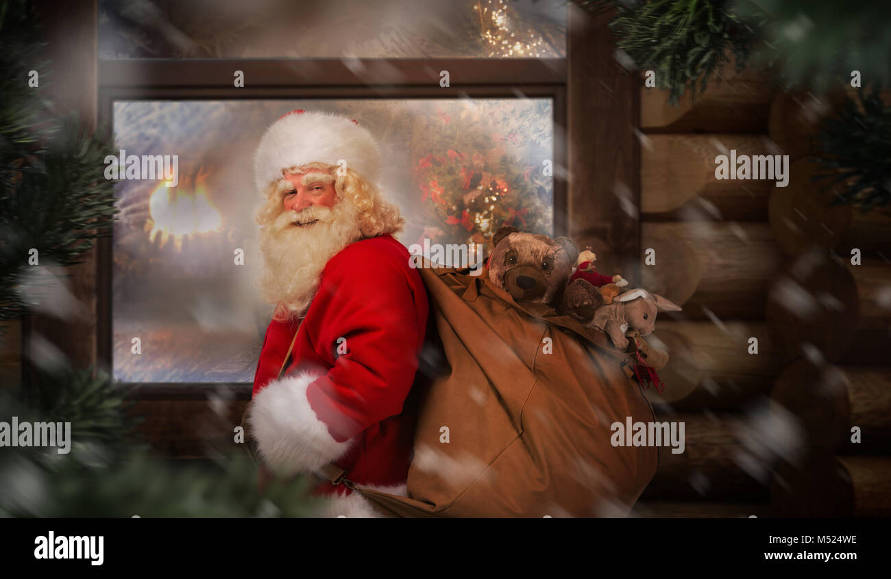Santa Claus carrying his sack near wooden house at night outdoor ...