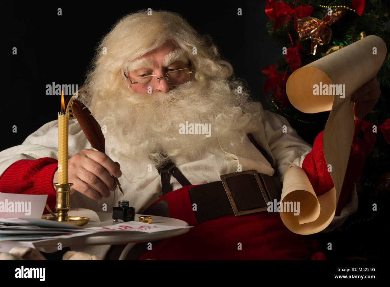 Santa Claus sitting at home and writing on old paper roll to do list ...