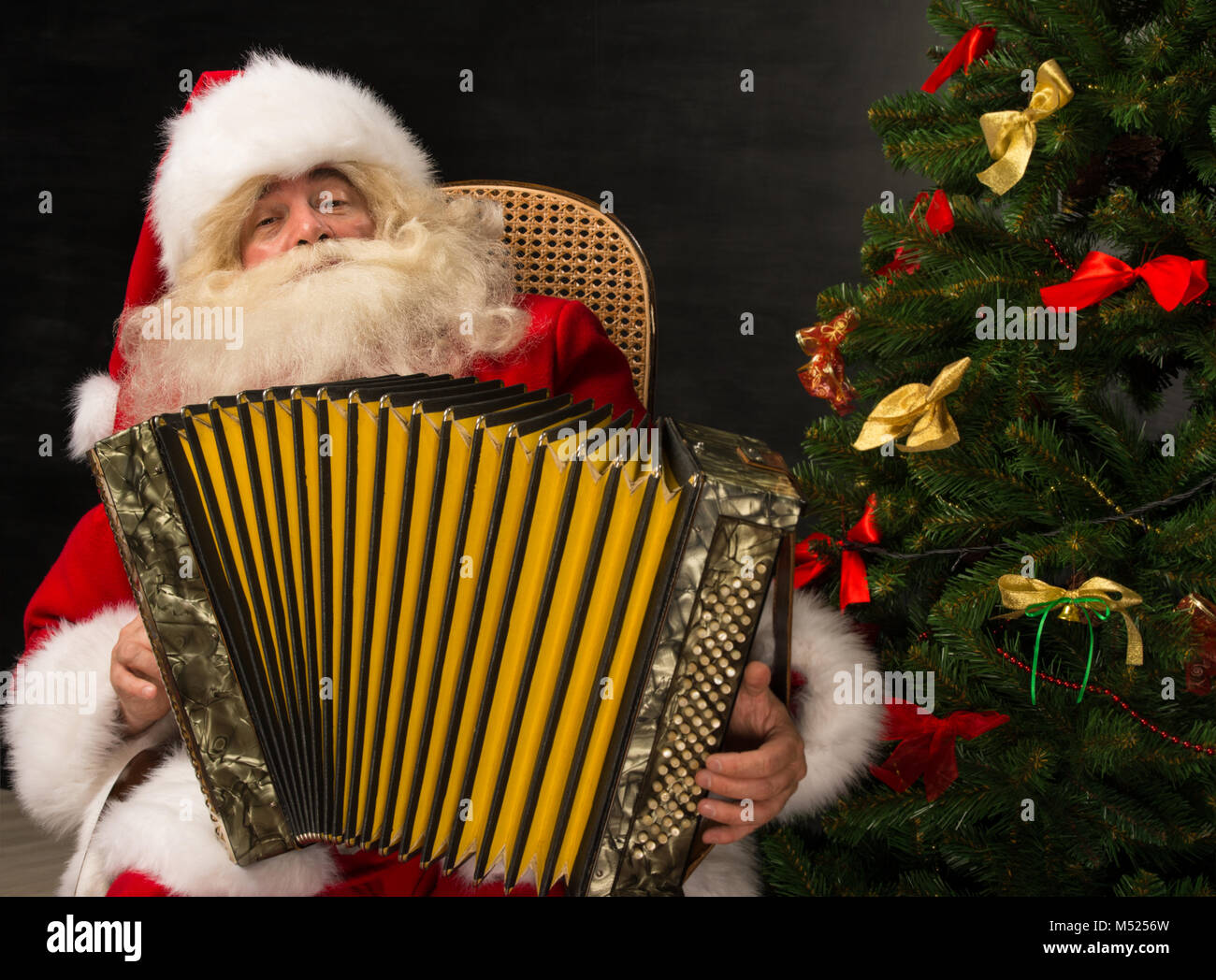 Santa Claus sitting in armchair near Christmas Tree at home and playing ...