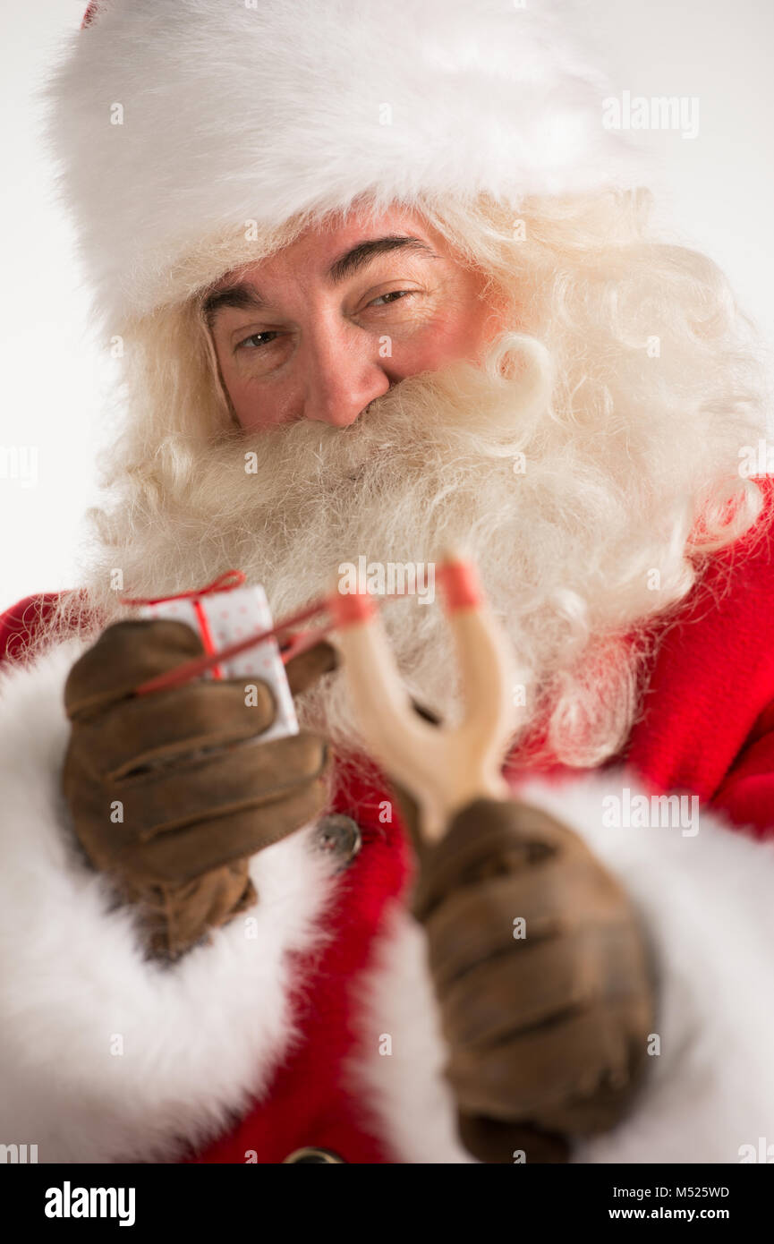 Portrait of happy Santa Claus aiming christmas gift with slingshot and ...