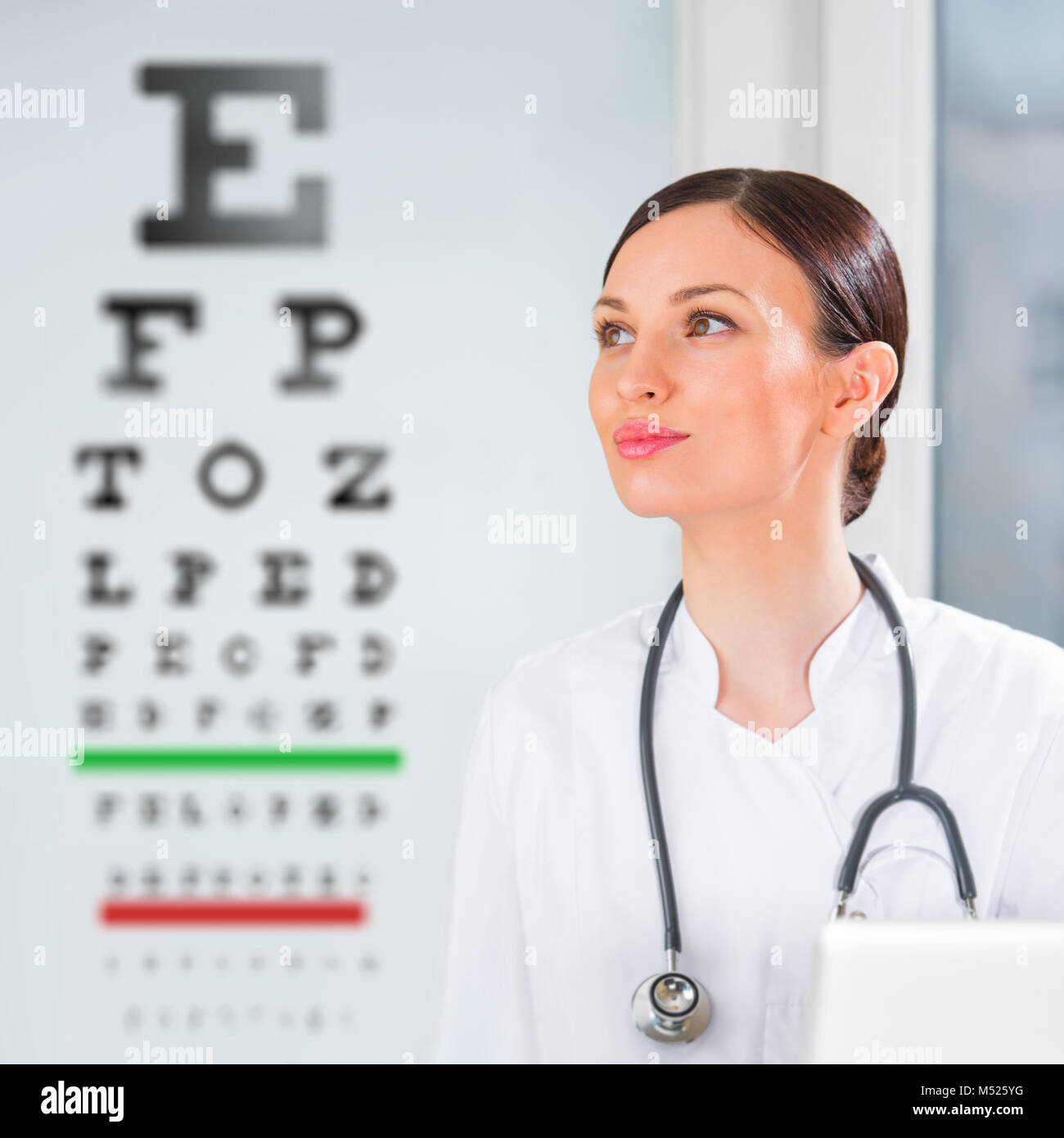 Female optician standing in front of eyesight test at hospital Stock ...