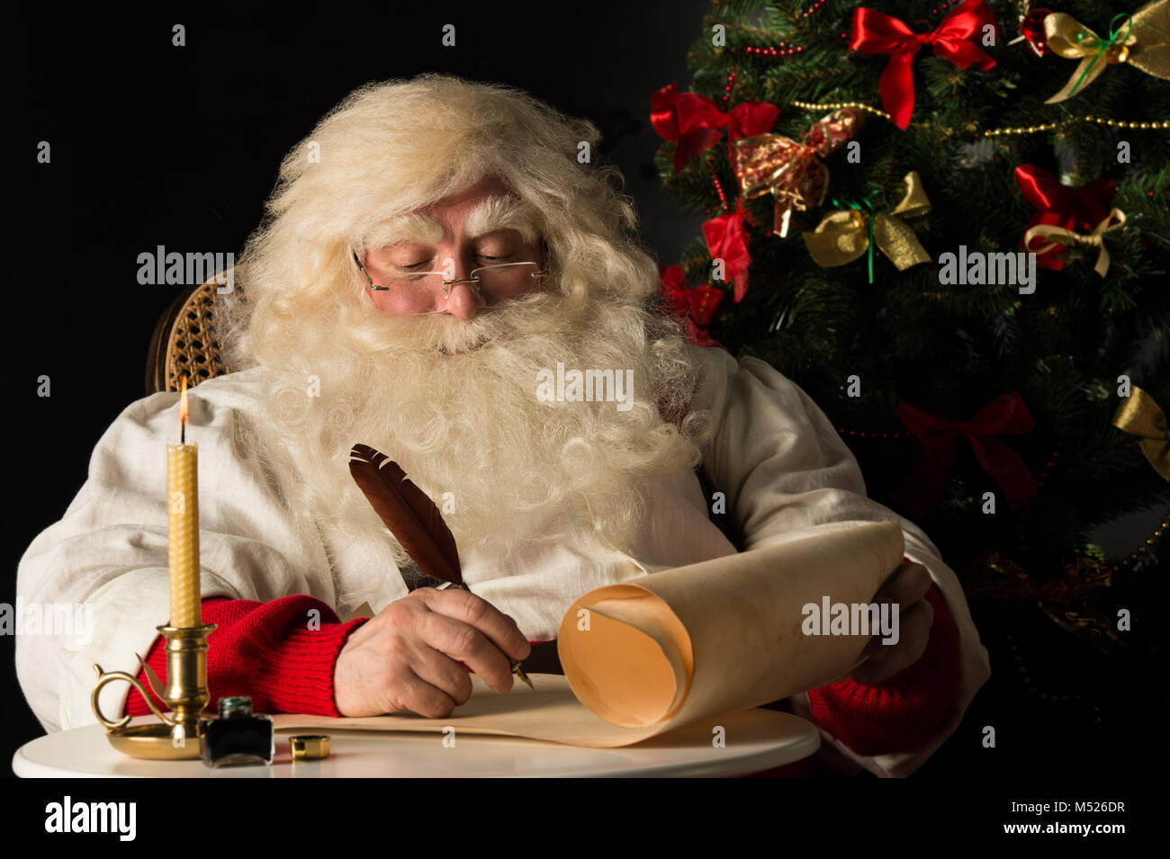 Santa Claus sitting at home and writing on old paper roll to do list ...