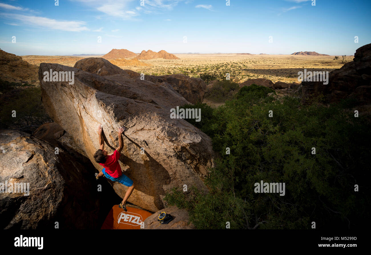 Man climbing boulder in Brandberg Massif with Namib Desert in ...