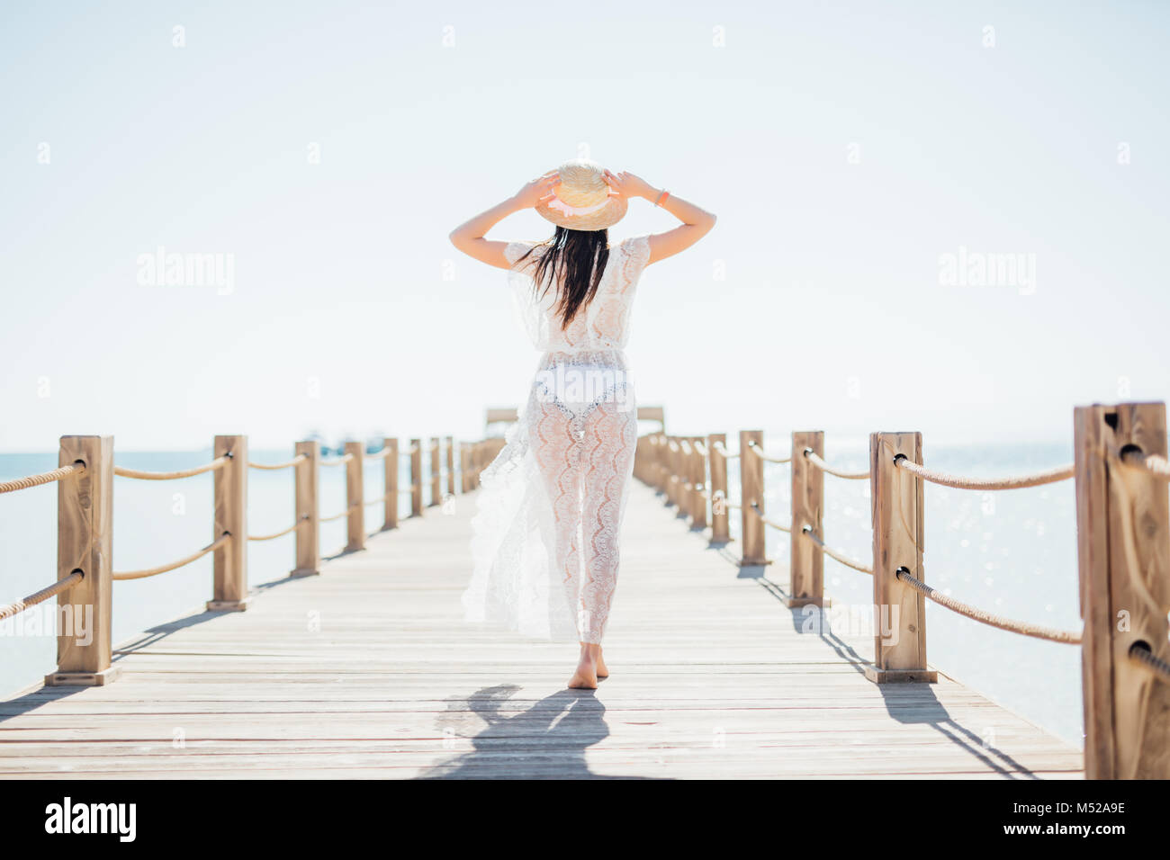 Back view of woman in bikini sunbathing on pier looking at the sea ...