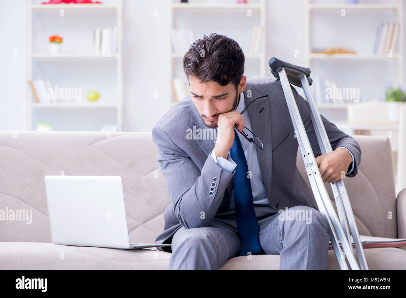 Businessman with crutches and broken leg at home working Stock Photo ...