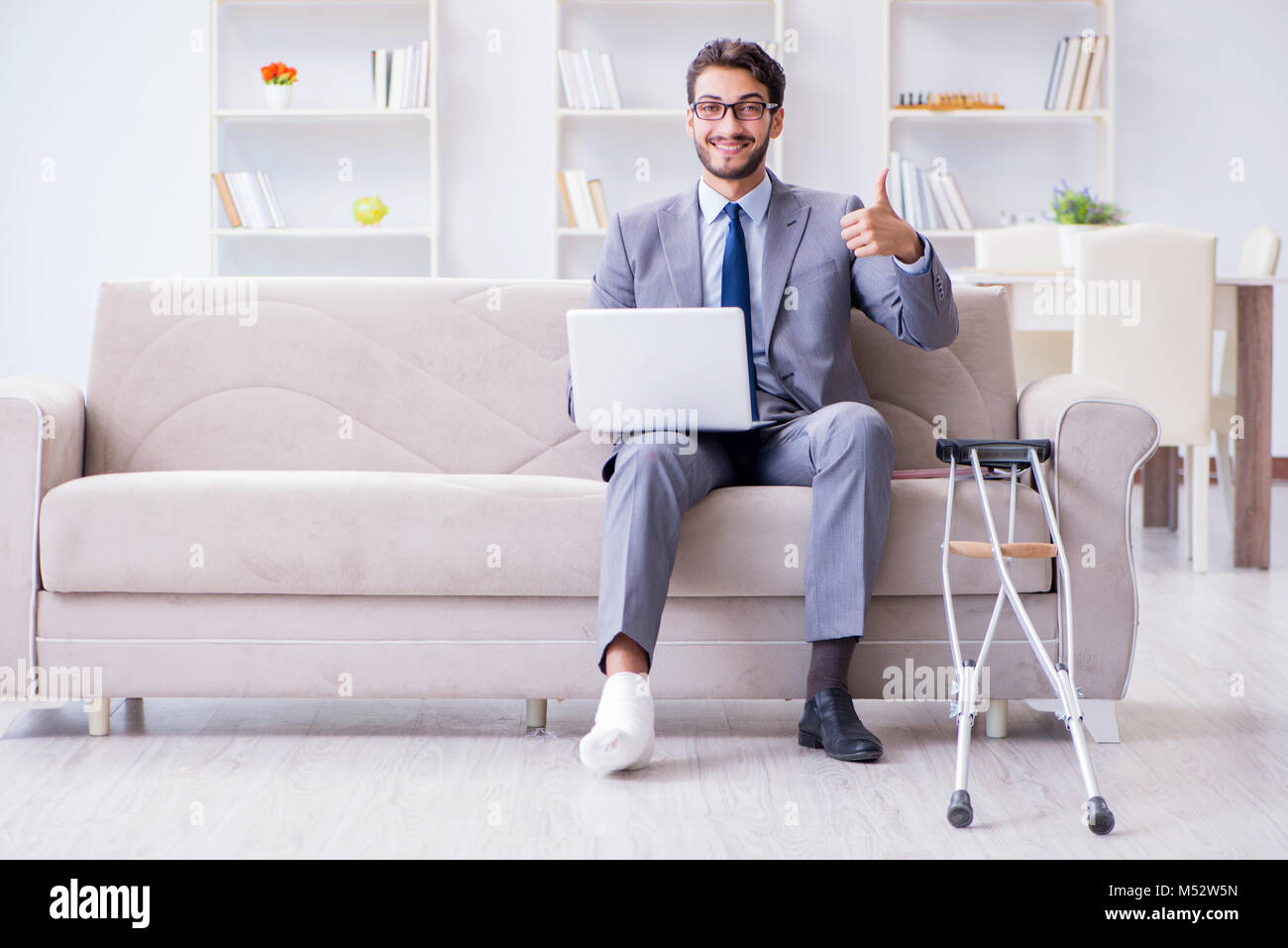Businessman with crutches and broken leg at home working Stock Photo ...