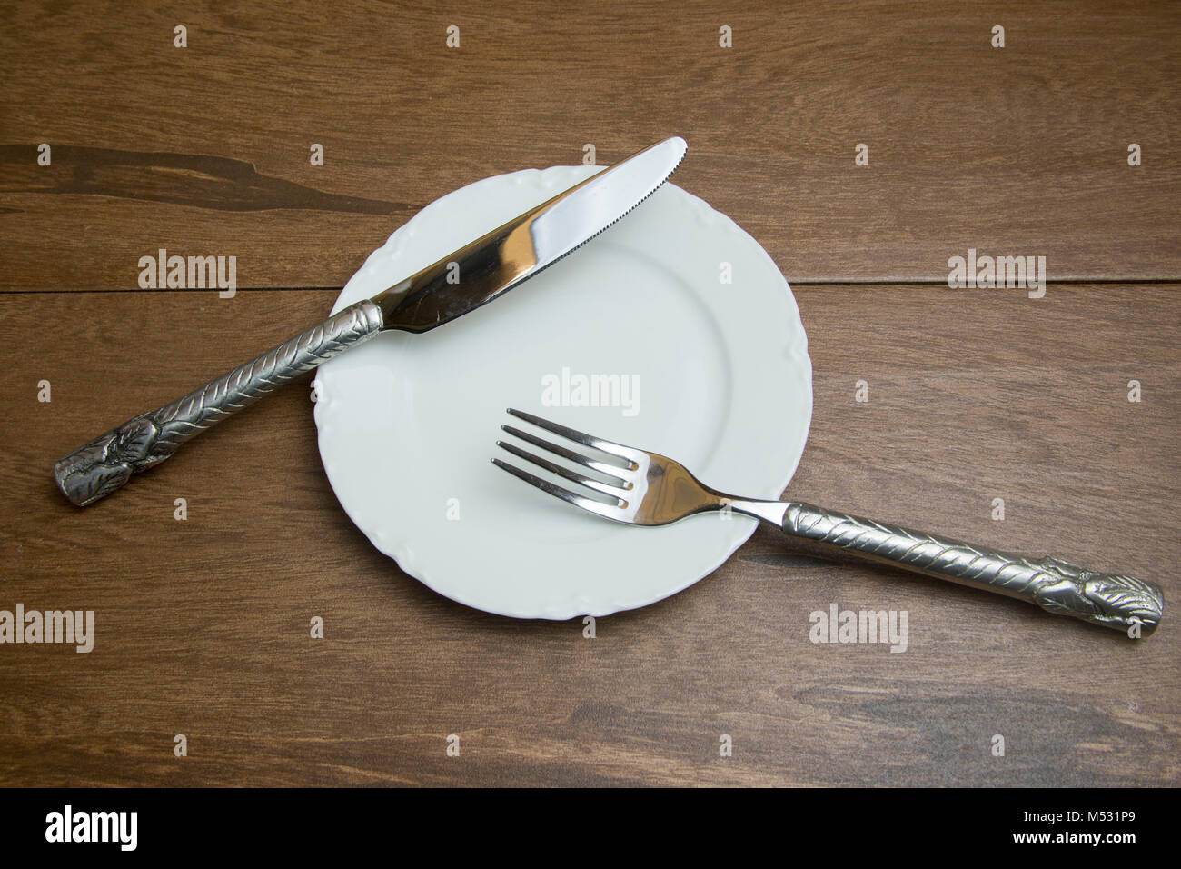 Empty white china plate with pewter knife and fork on wooden boards ...
