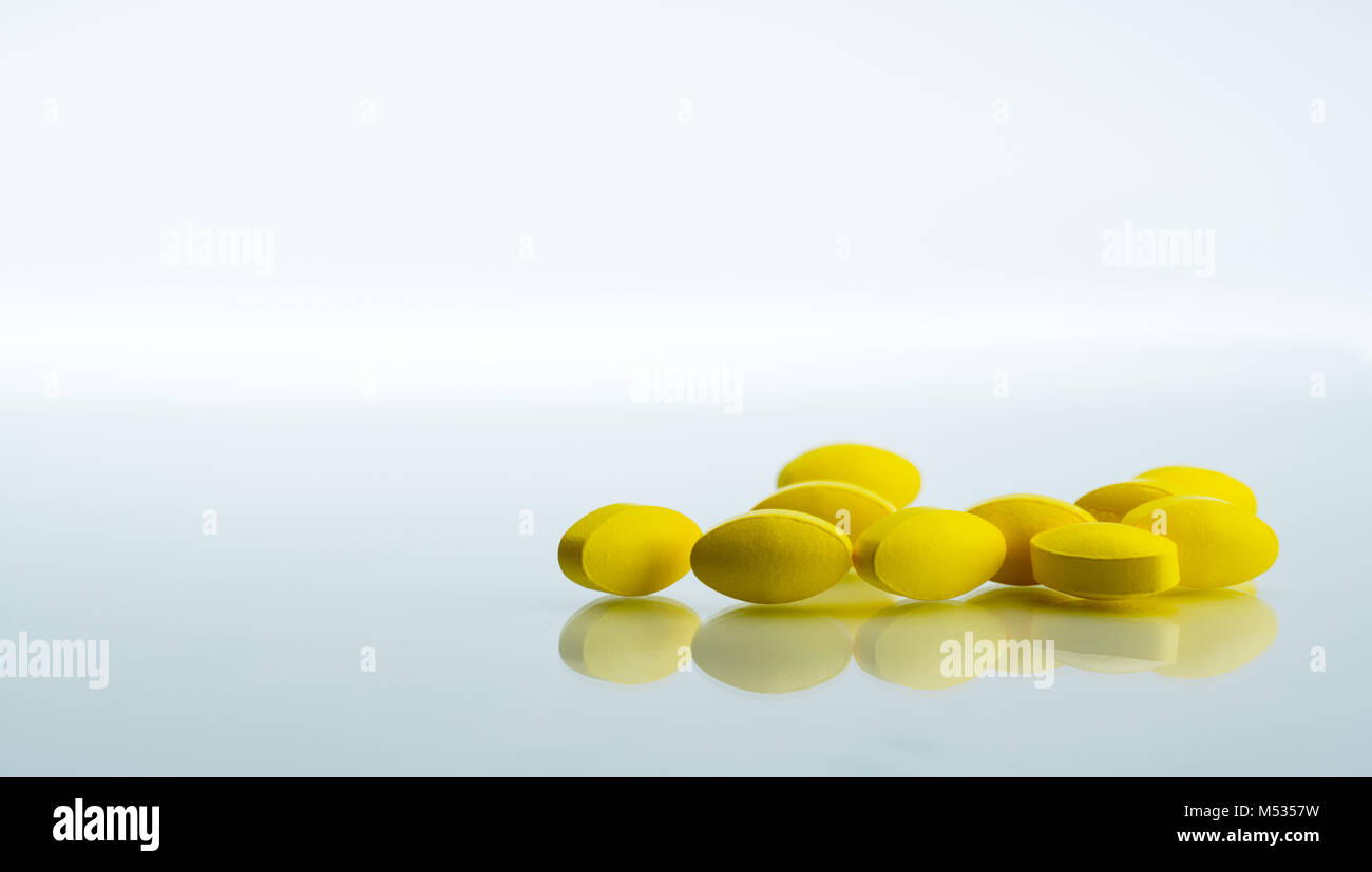 Pile of yellow oval tablet pills on white background with copy space ...