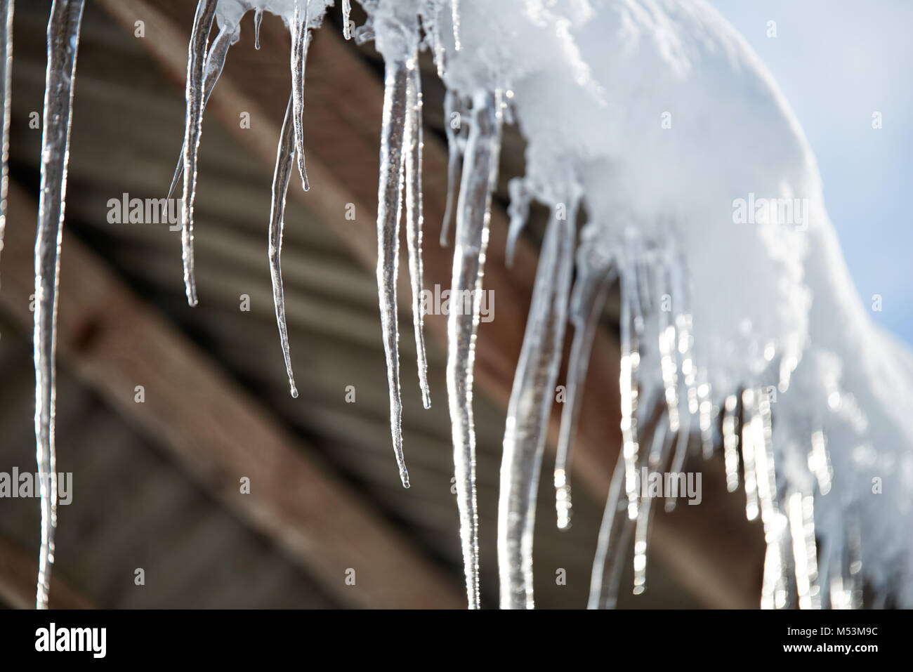 Icicles and Snow Overhanging a Roof. Row of long and big icicles on the ...