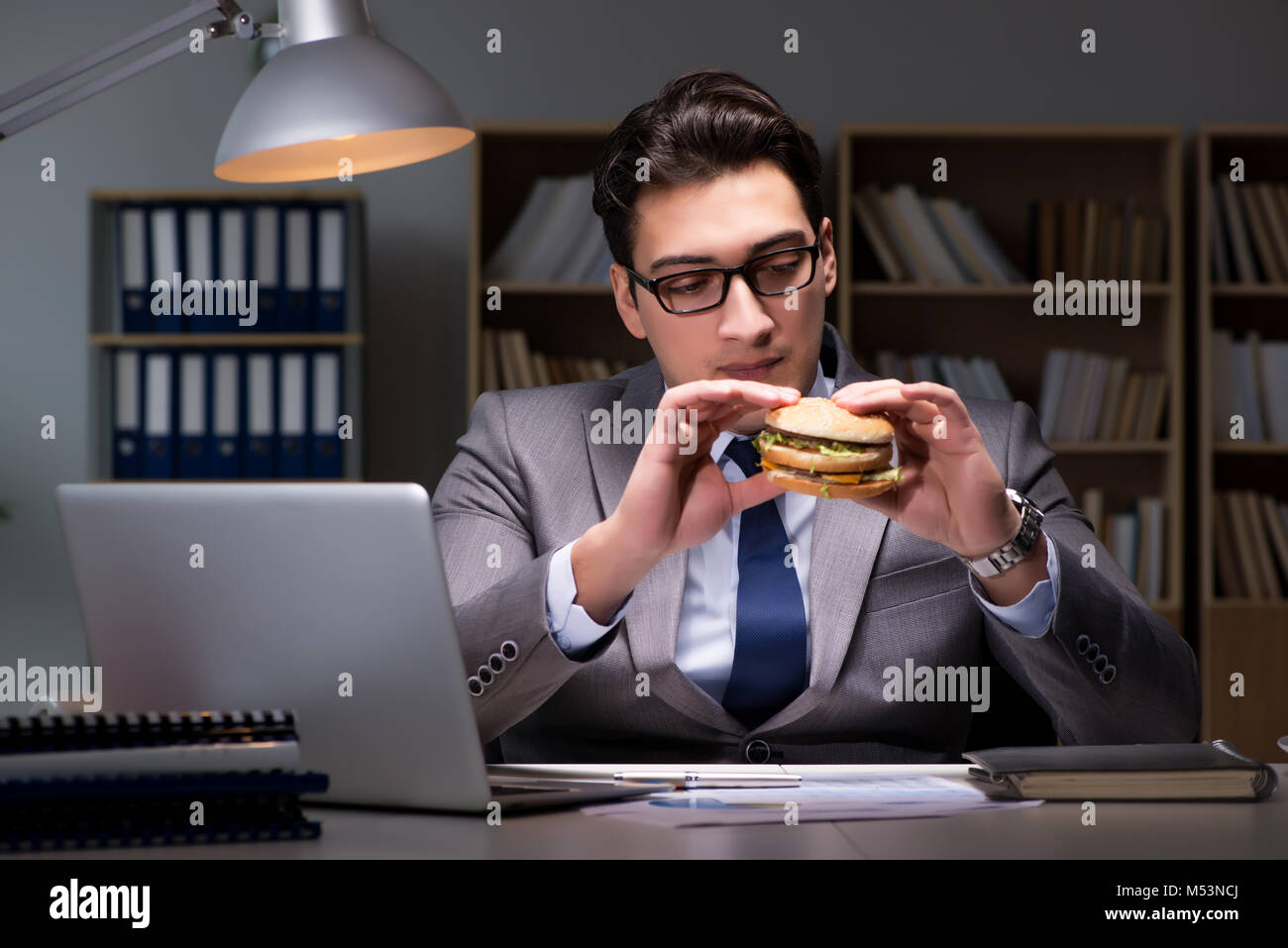 Businessman late at night eating a burger Stock Photo - Alamy