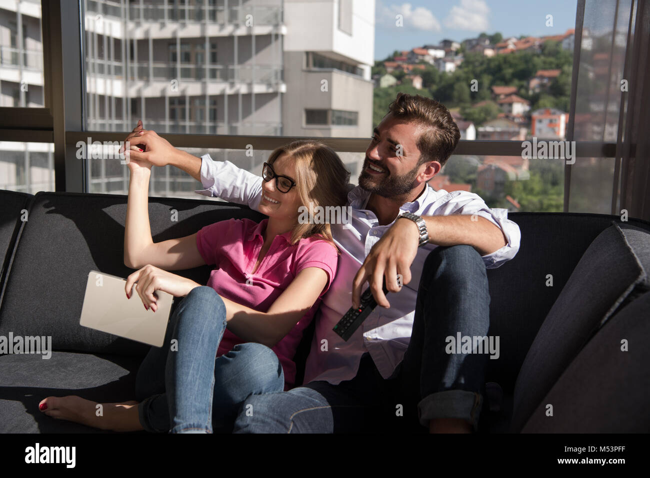 Young couple sitting on sofa near the window watching television ...