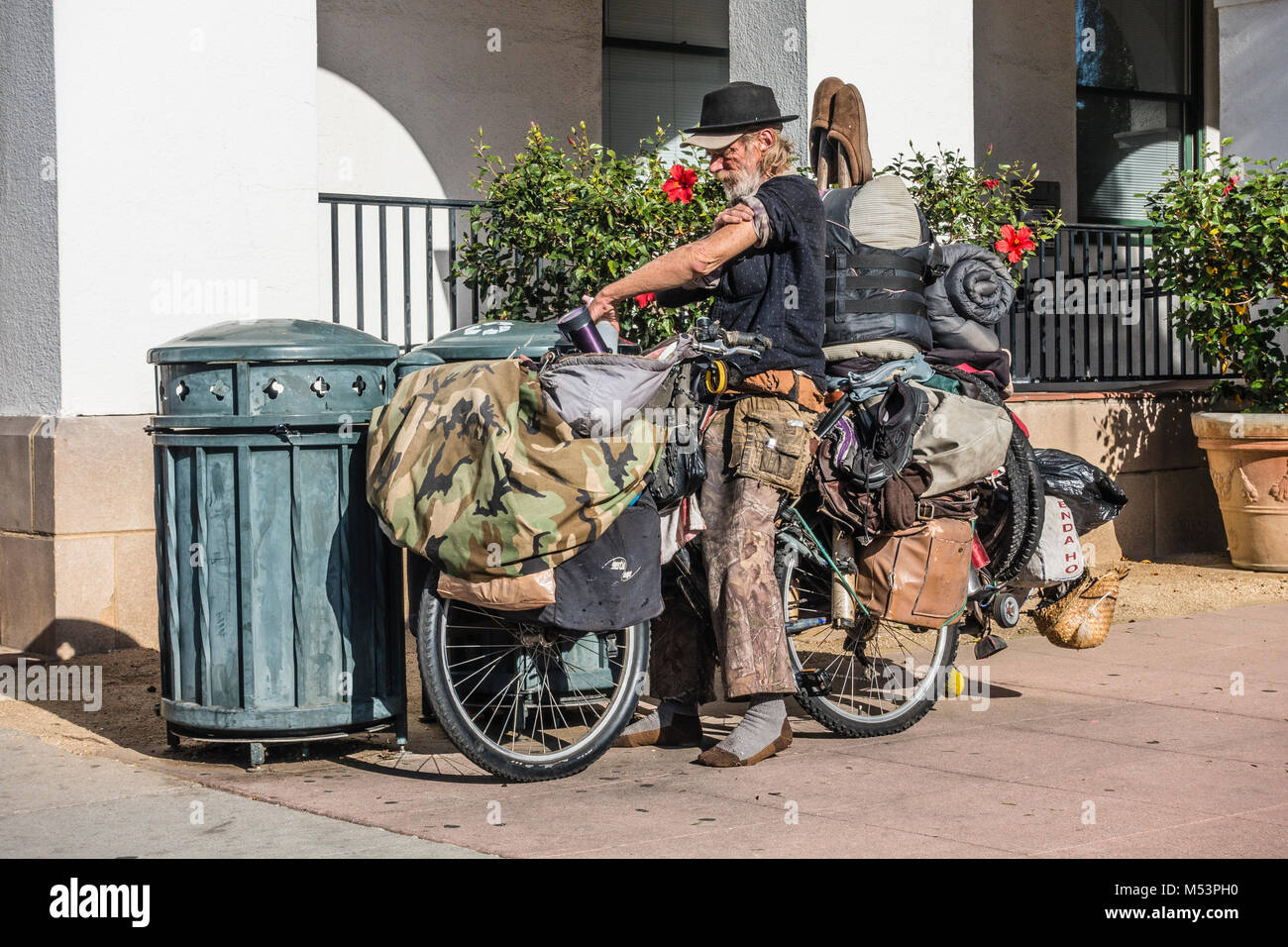 A homeless male on his bicycle loaded with his worldly possessions is ...