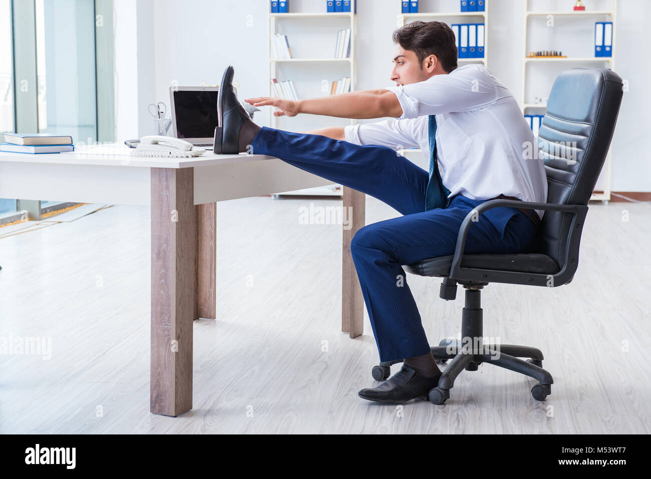 Young businessman doing sports stretching at workplace Stock Photo - Alamy