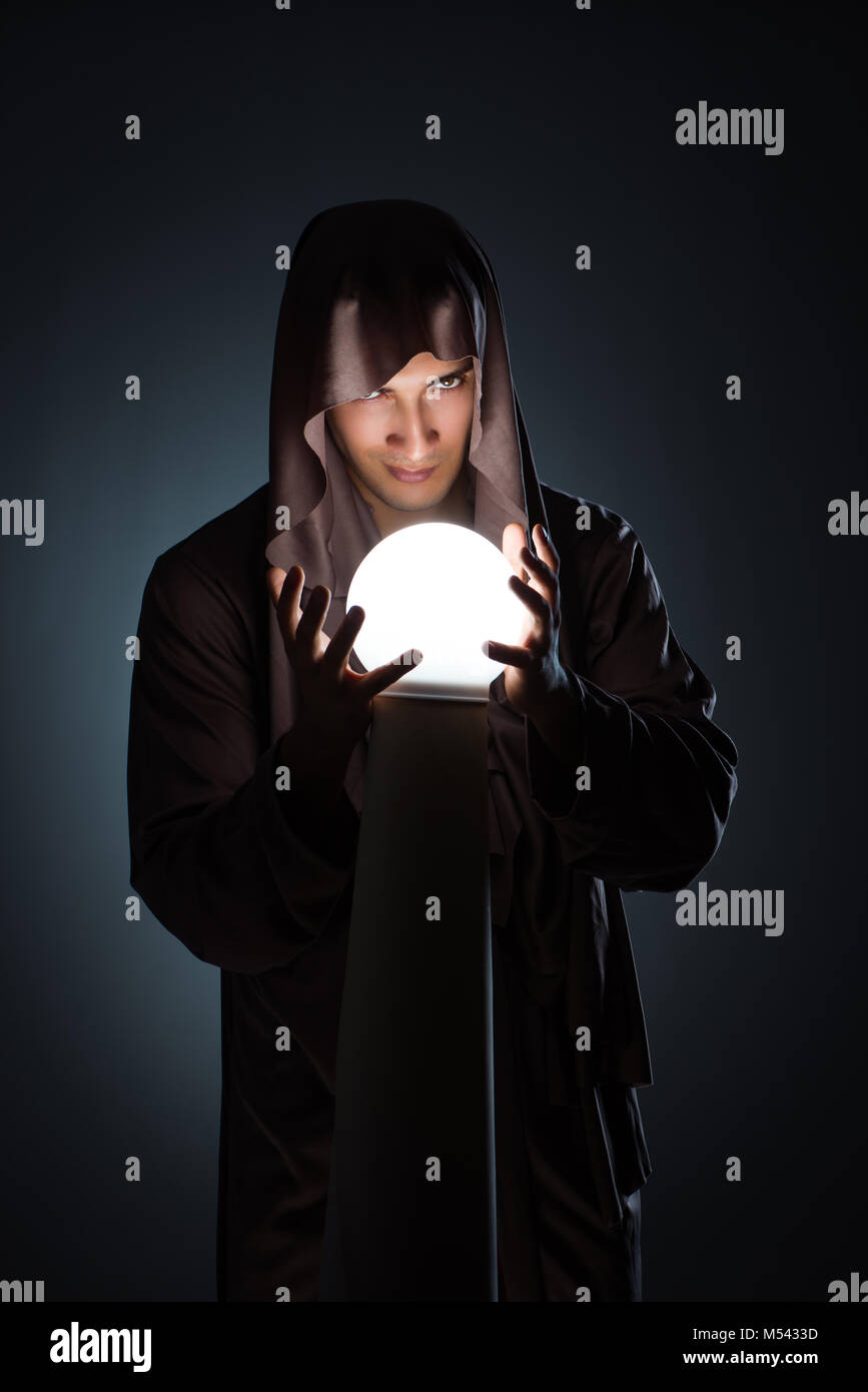 Young wizard with crystal ball in dark room Stock Photo - Alamy