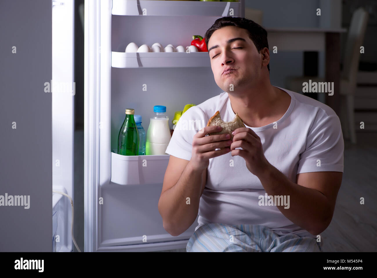 Man at the fridge eating at night Stock Photo - Alamy