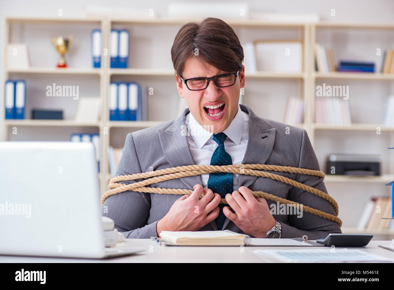 Businessman tied up with rope in office Stock Photo - Alamy