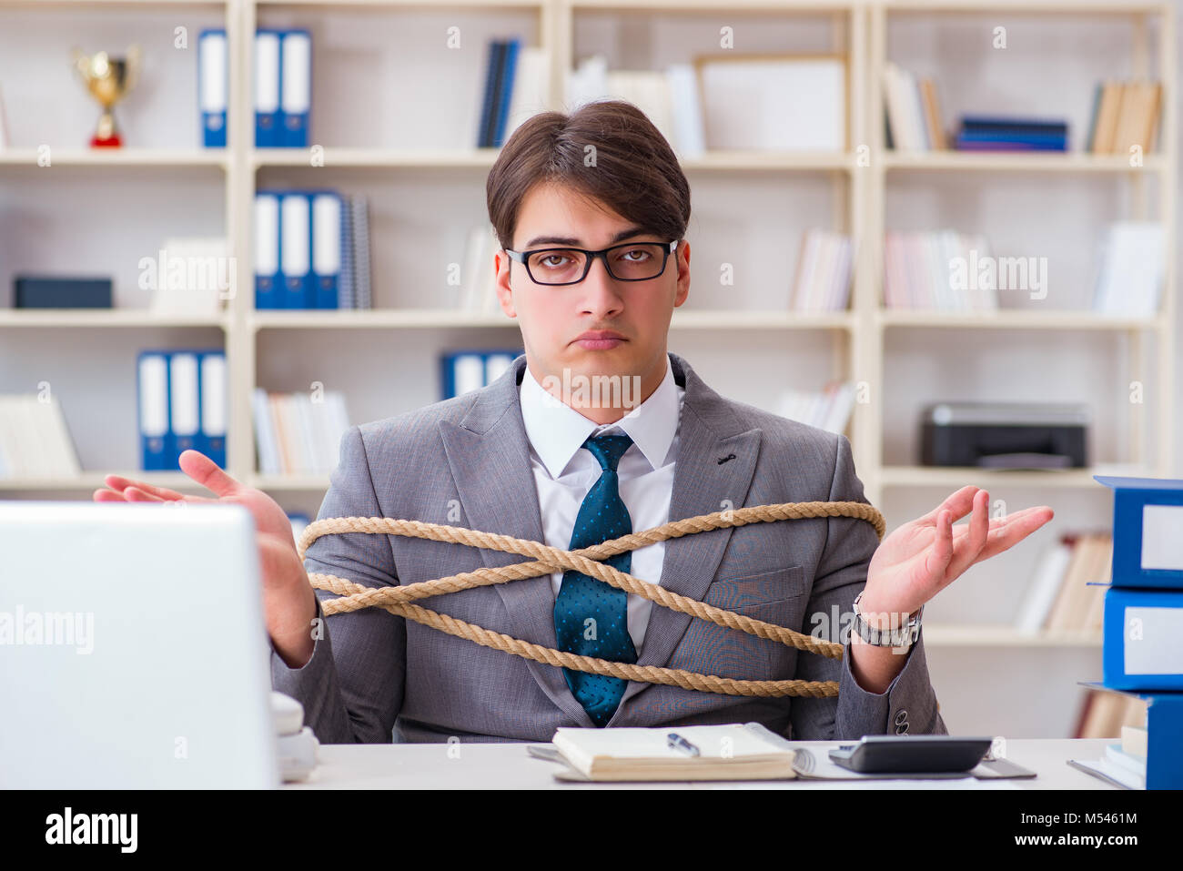 Businessman tied up with rope in office Stock Photo - Alamy