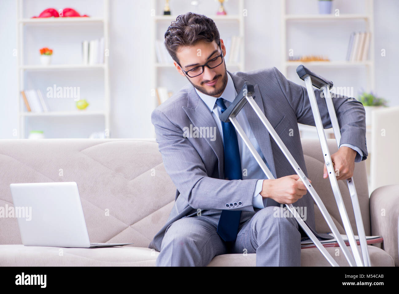Businessman with crutches and broken leg at home working Stock Photo ...
